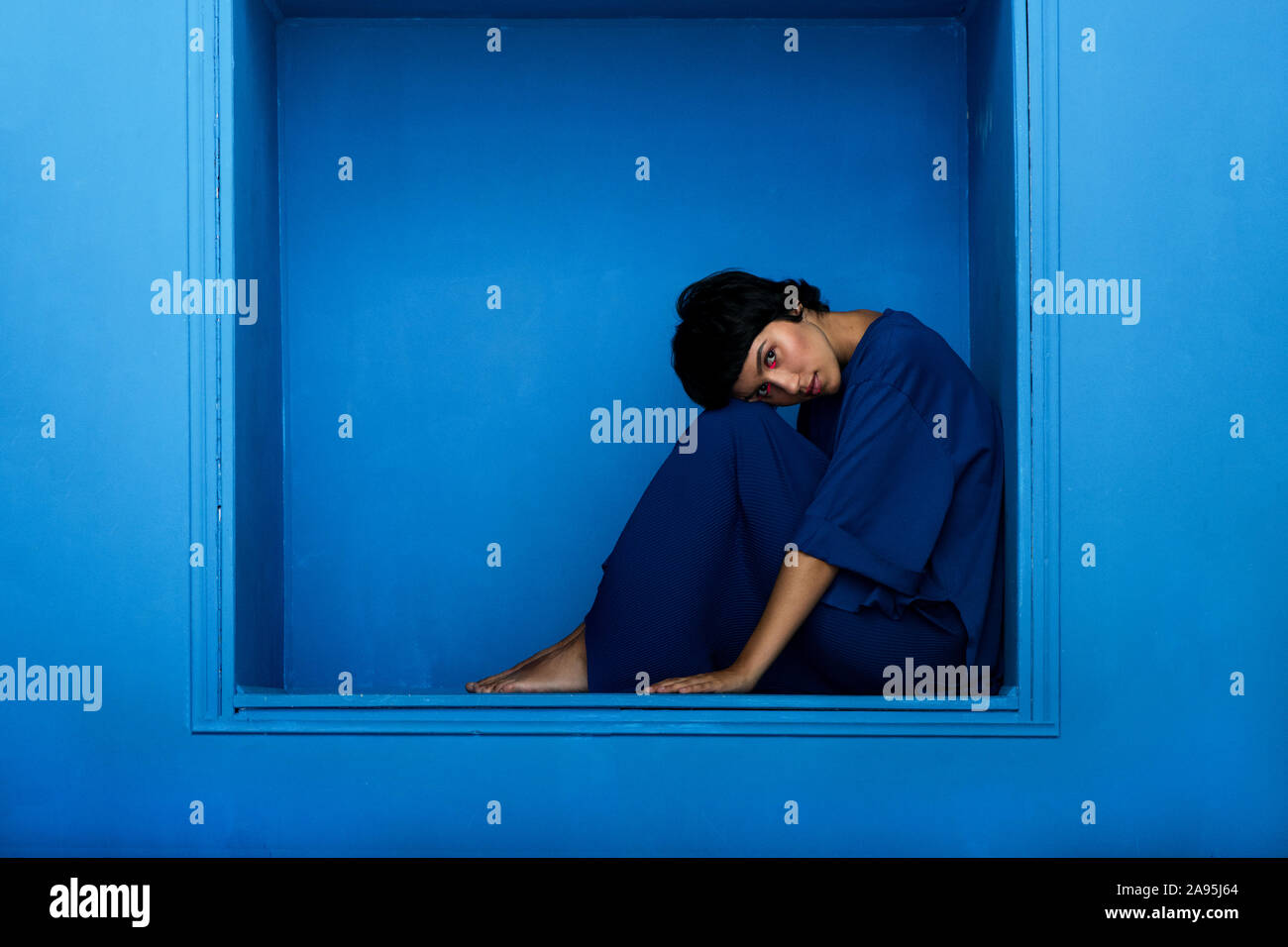 Young beautiful woman sitting in niche on blue background. Studio shot ...