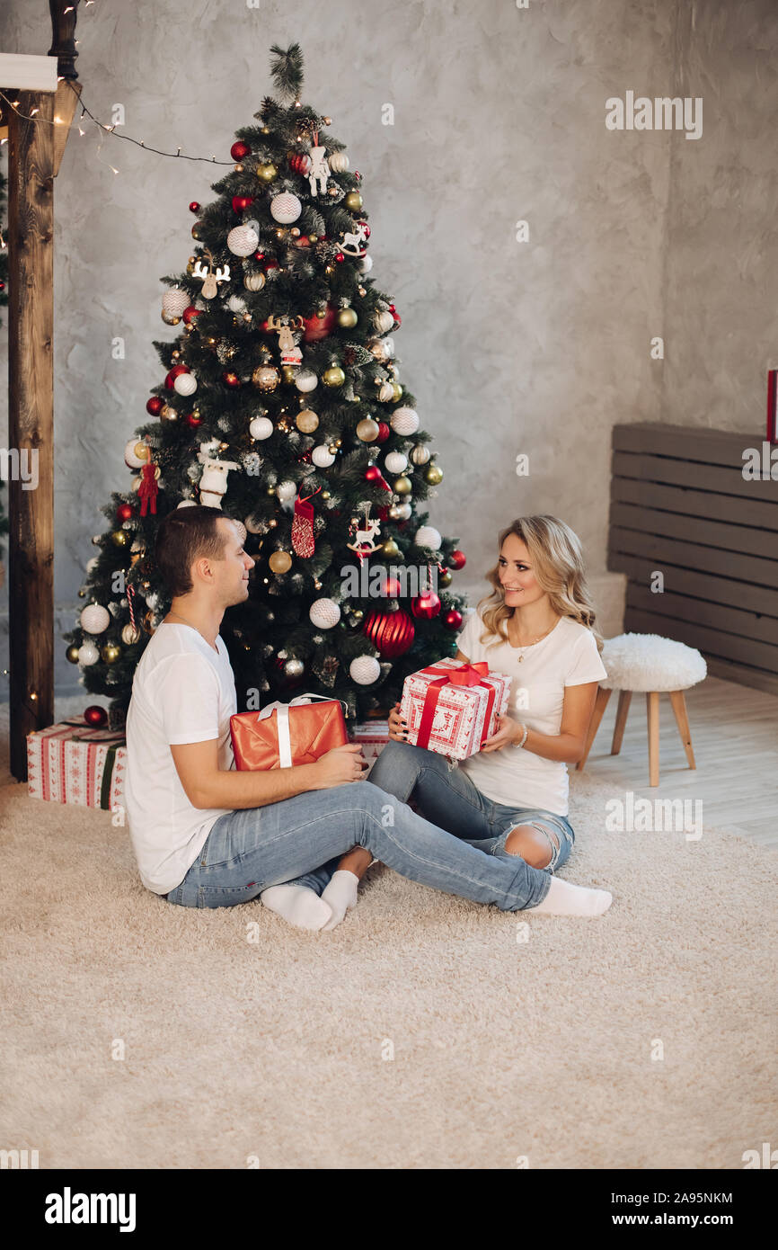 Loving couple sorting presents by Christmas tree Stock Photo - Alamy