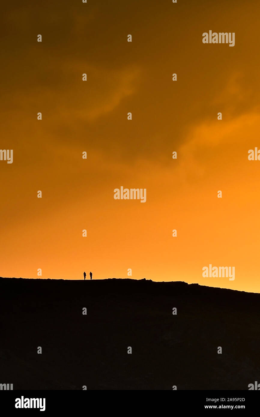 The tiny figures of two walkers silhouetted against an intense sunset ...