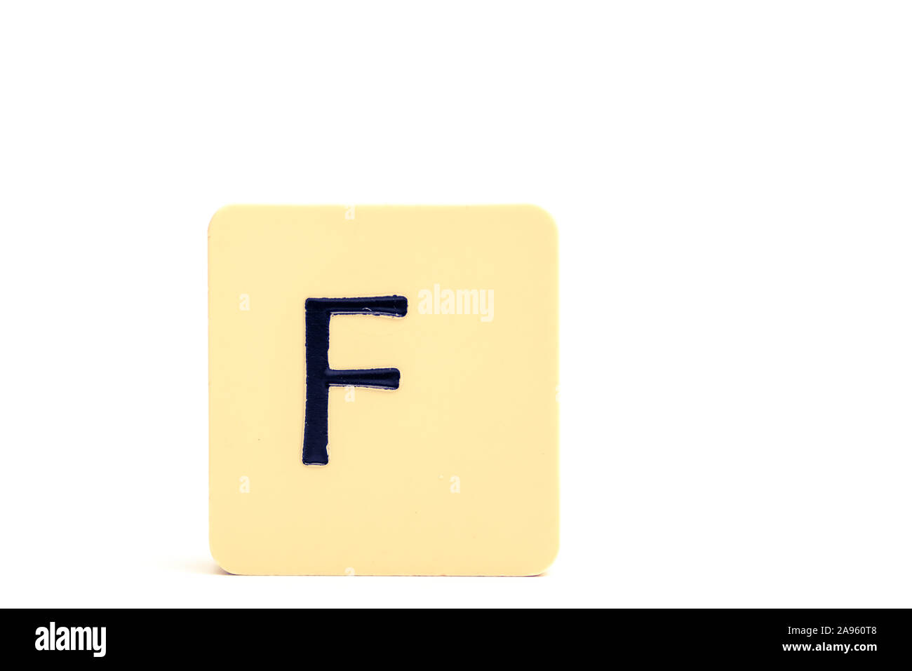 Dark letter F on a pale yellow square block isolated on white ...