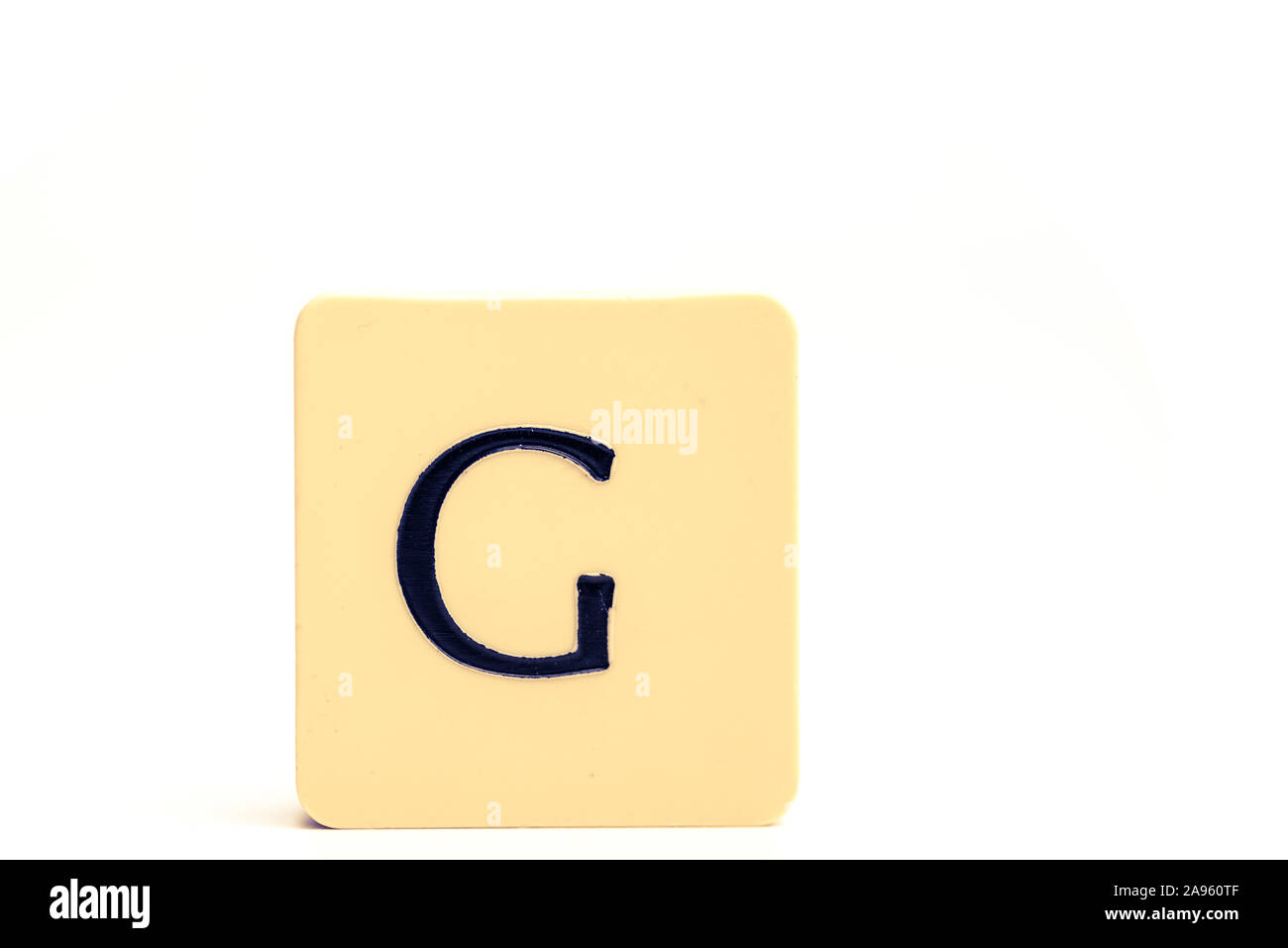 Dark letter G on a pale yellow square block isolated on white ...