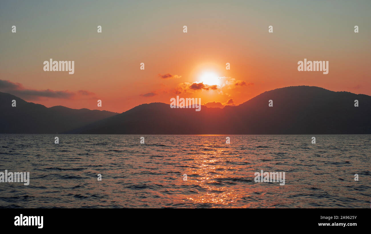 Beautiful sunset on the sea, the sun behind the horizon with mountains ...