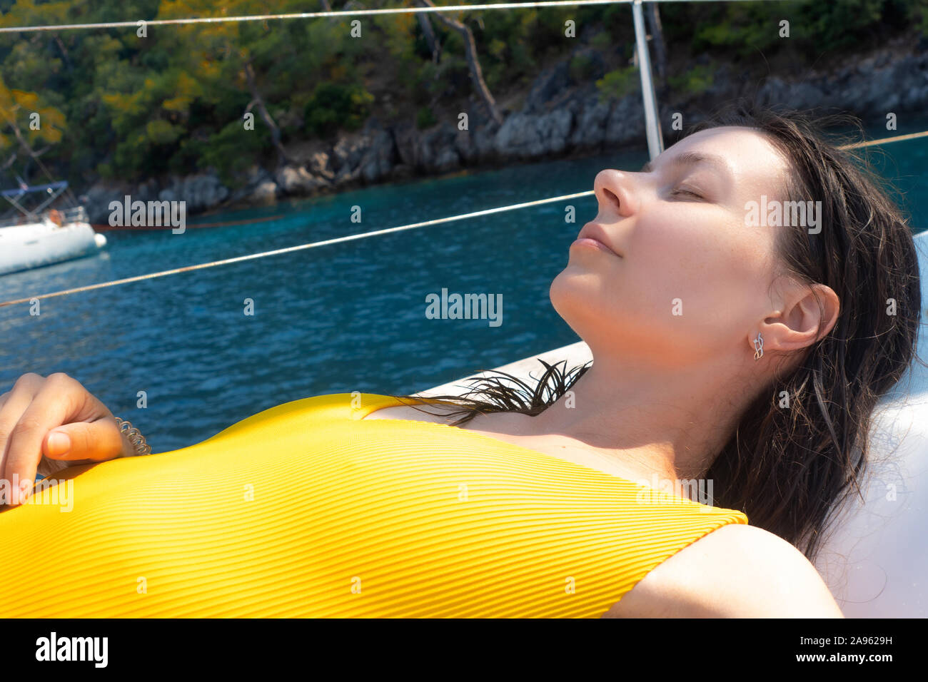 Young Woman In A Bright Yellow One Piece Swimsuit Sunbathing On The
