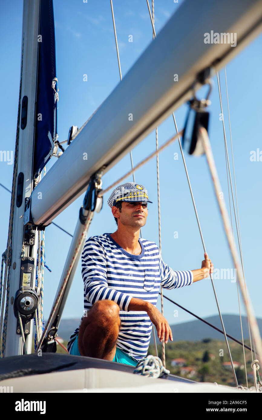 Handsome young man with captain cap on a sailboat at sea on a suuny day ...