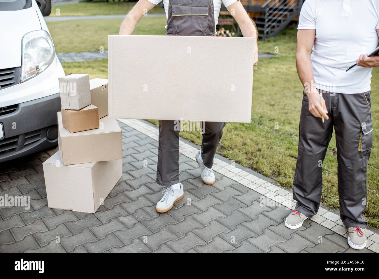 Delivery men moving cardboard boxes outdoors, delivering goods with ...