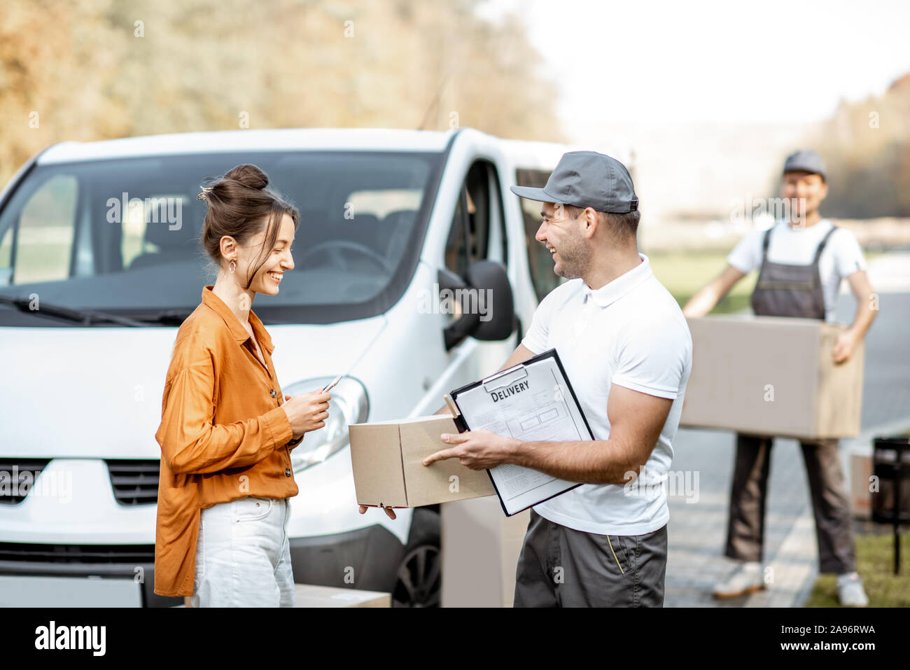 Courier with checklist delivering goods to a young woman by cargo van ...
