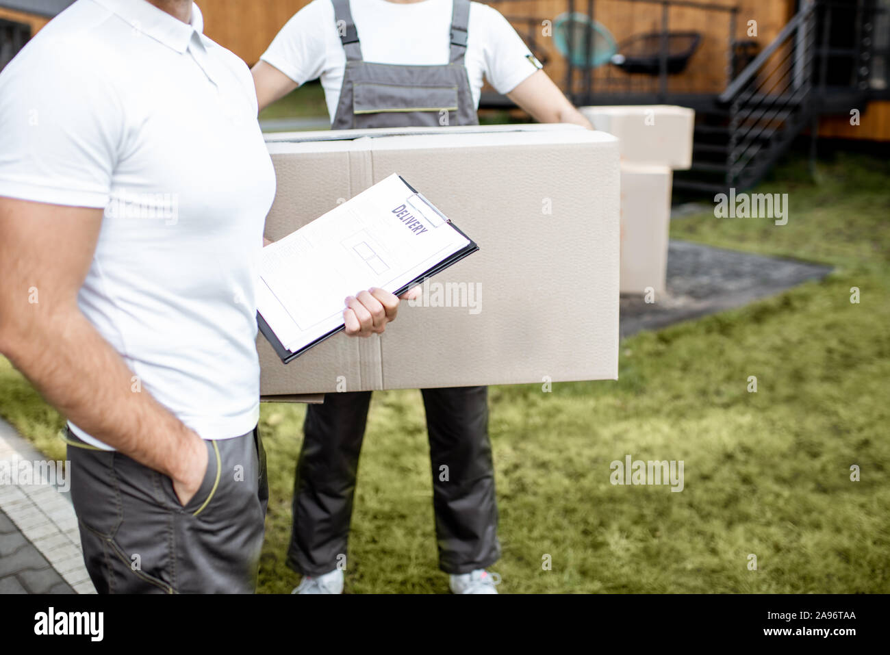 Delivery men with checklist and cardboard boxes outdoors, close-up view ...