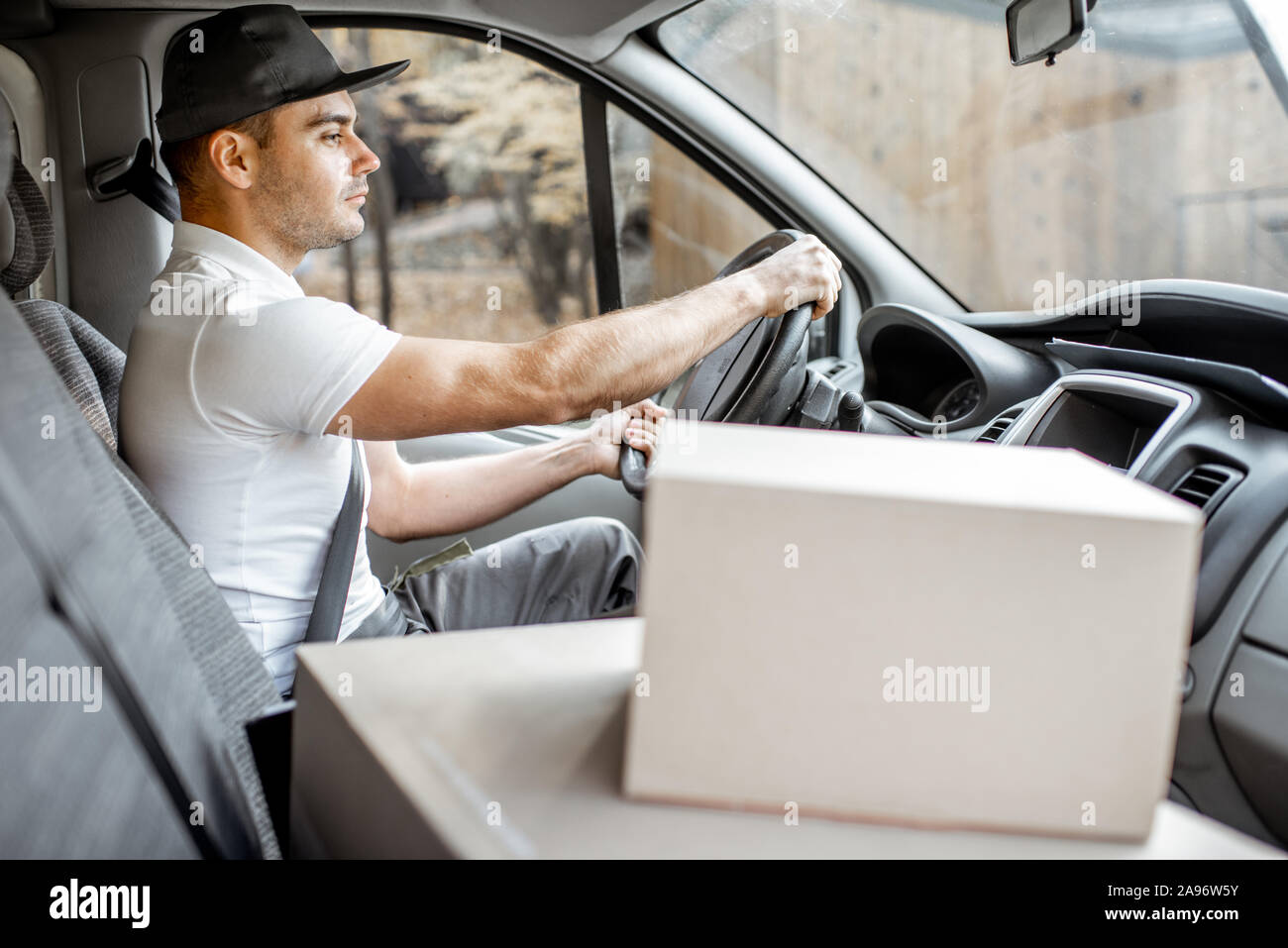 Delivery man driving cargo vehicle with parcels on the passenger seat ...