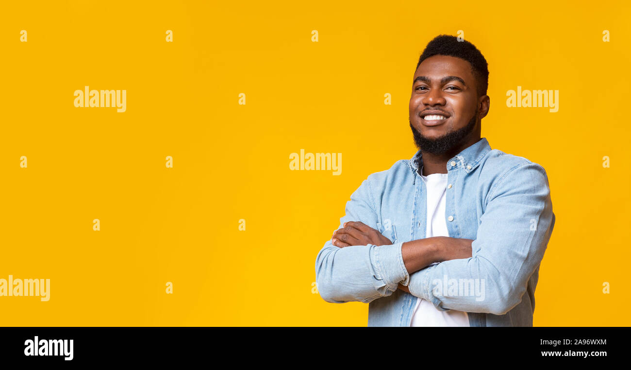 Portrait of attractive african american man with folded arms over yellow background, panorama ...