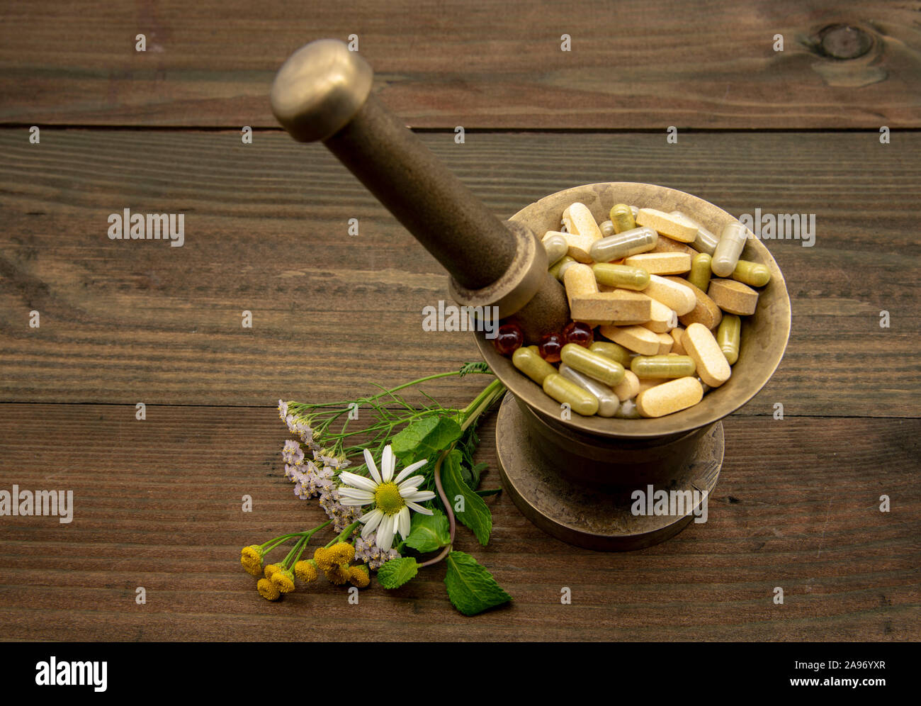 A copper mortar full of capsules and pills. Nearby lie medicinal herbs ...