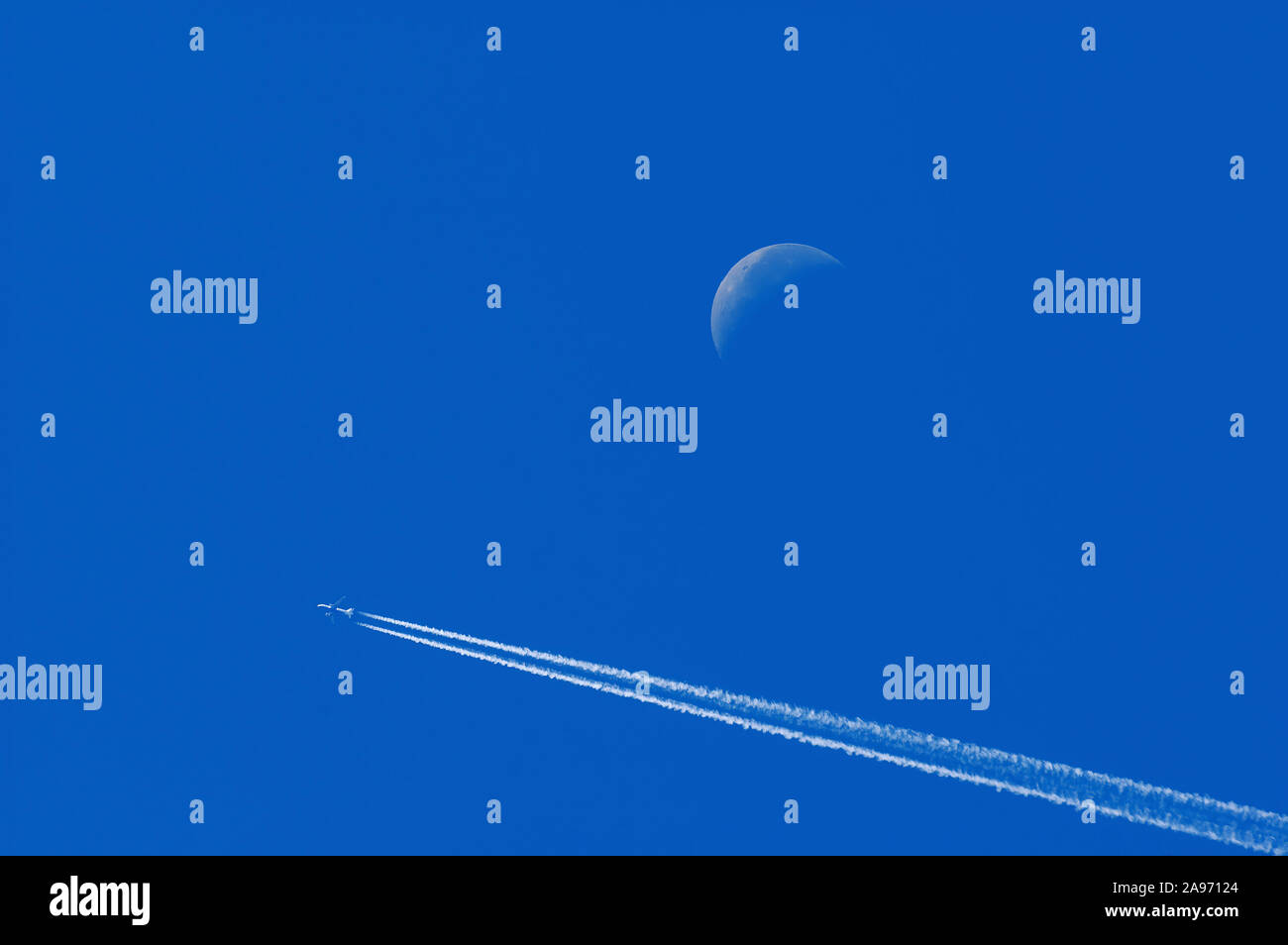 Flying commercial airliner passes by a crescent moon in a deep blue sky ...