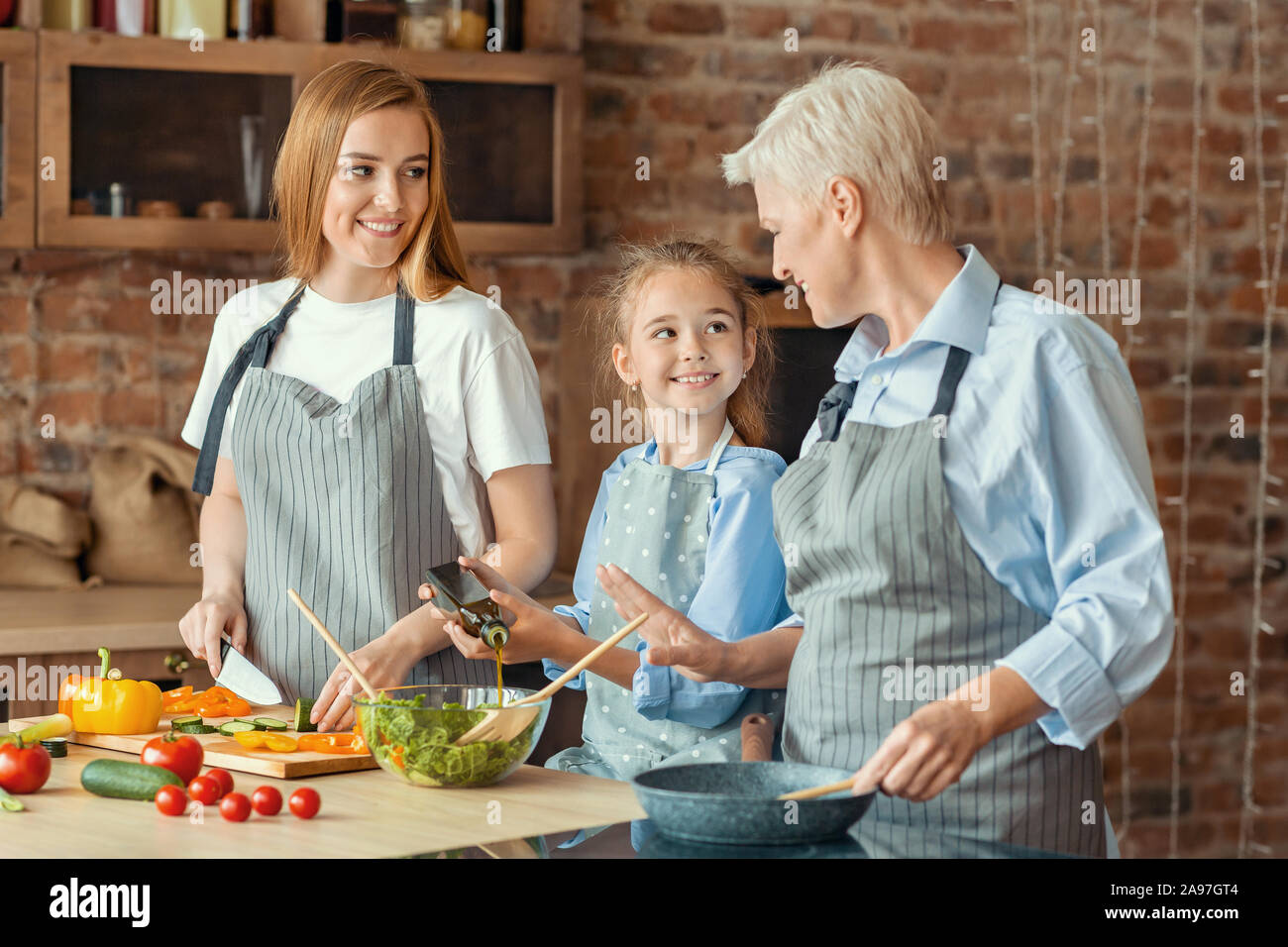 Little girl happy to help mother and granny cooking healthy dinner ...
