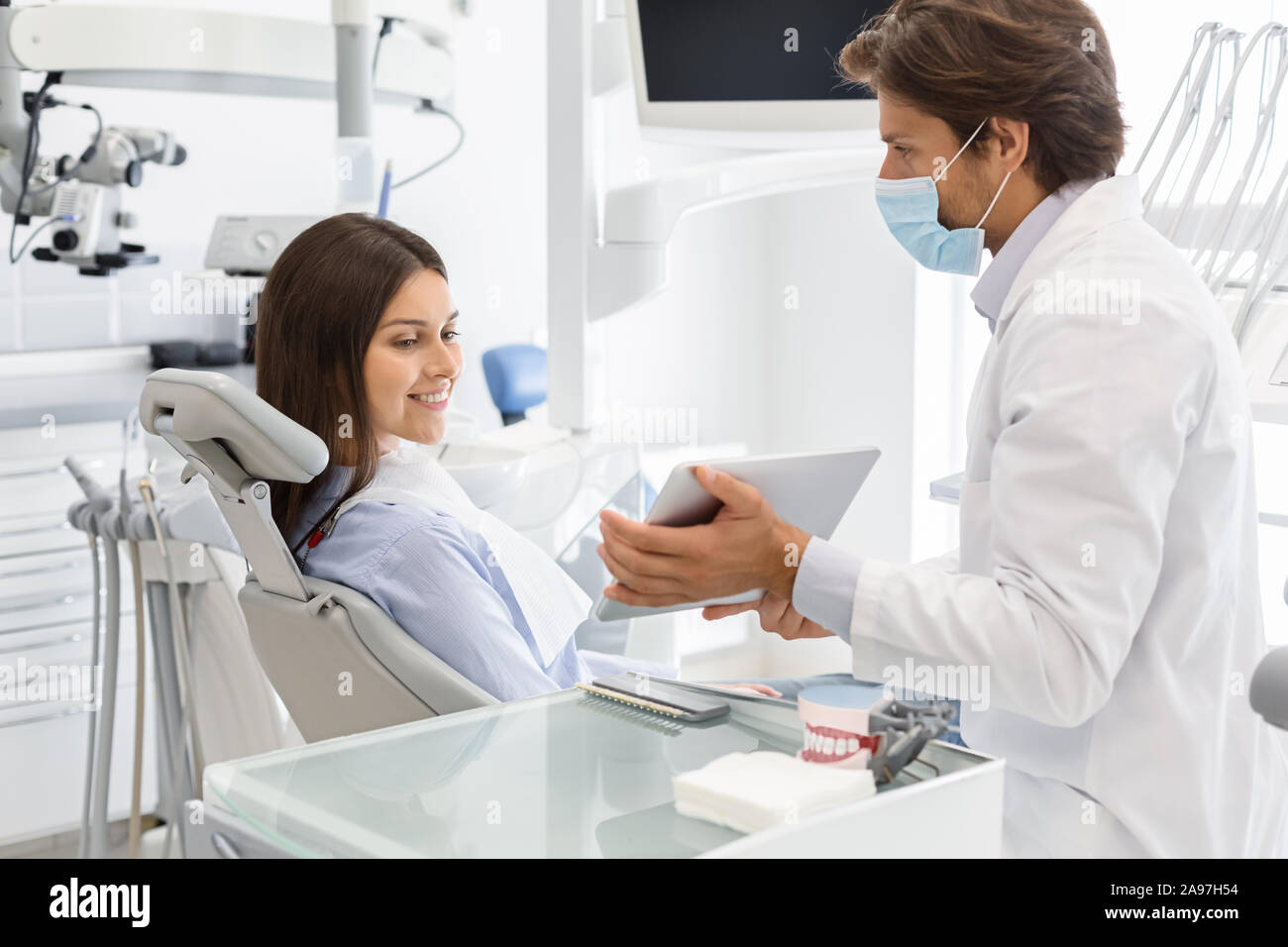 Male dentist showing patient results of treatment on digital tablet, dental cabinet, copy space ...