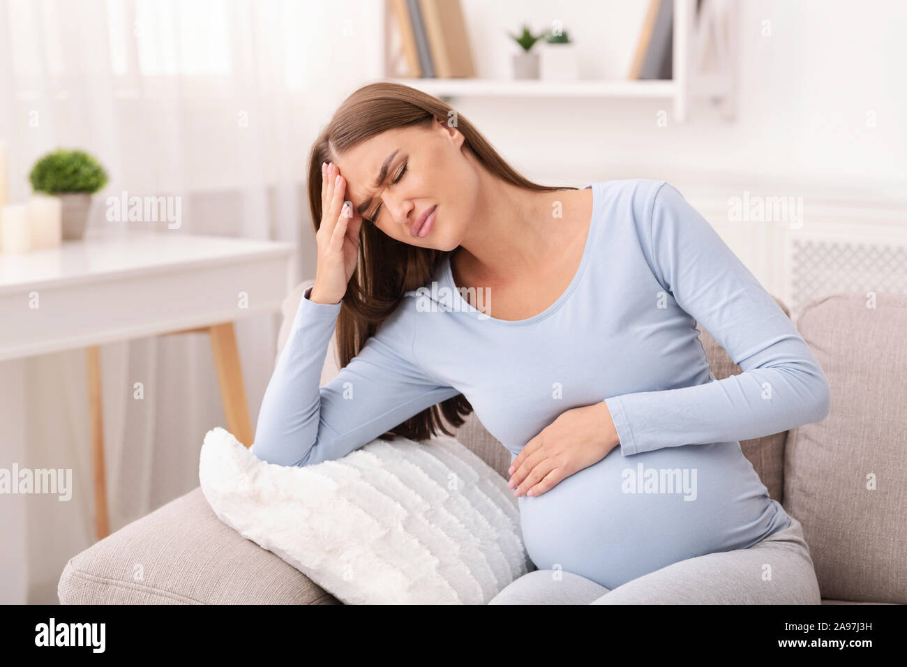 Pregnant Lady Having Headache Touching Head Sitting On Couch Indoor 2190
