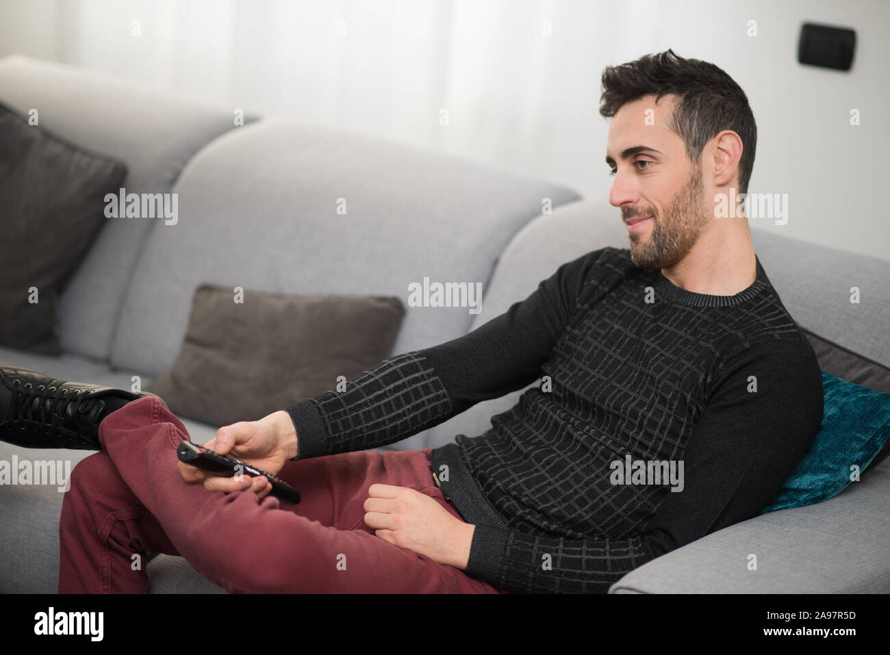 Portrait of a smiling man choosing a program to watch on television at ...