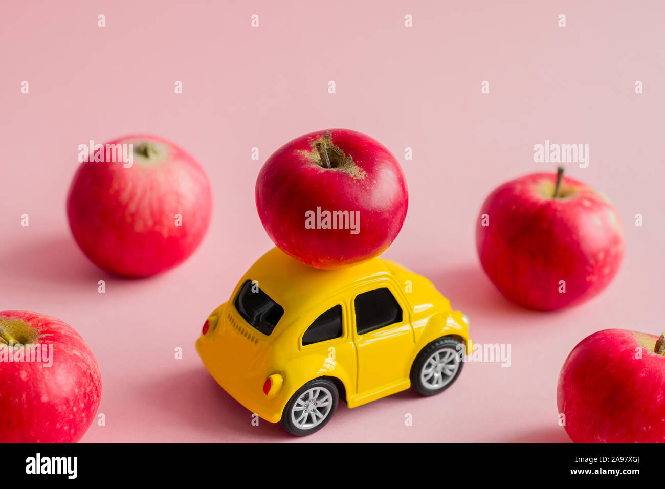 little yellow bauble car with red apples on a pastel pink background ...