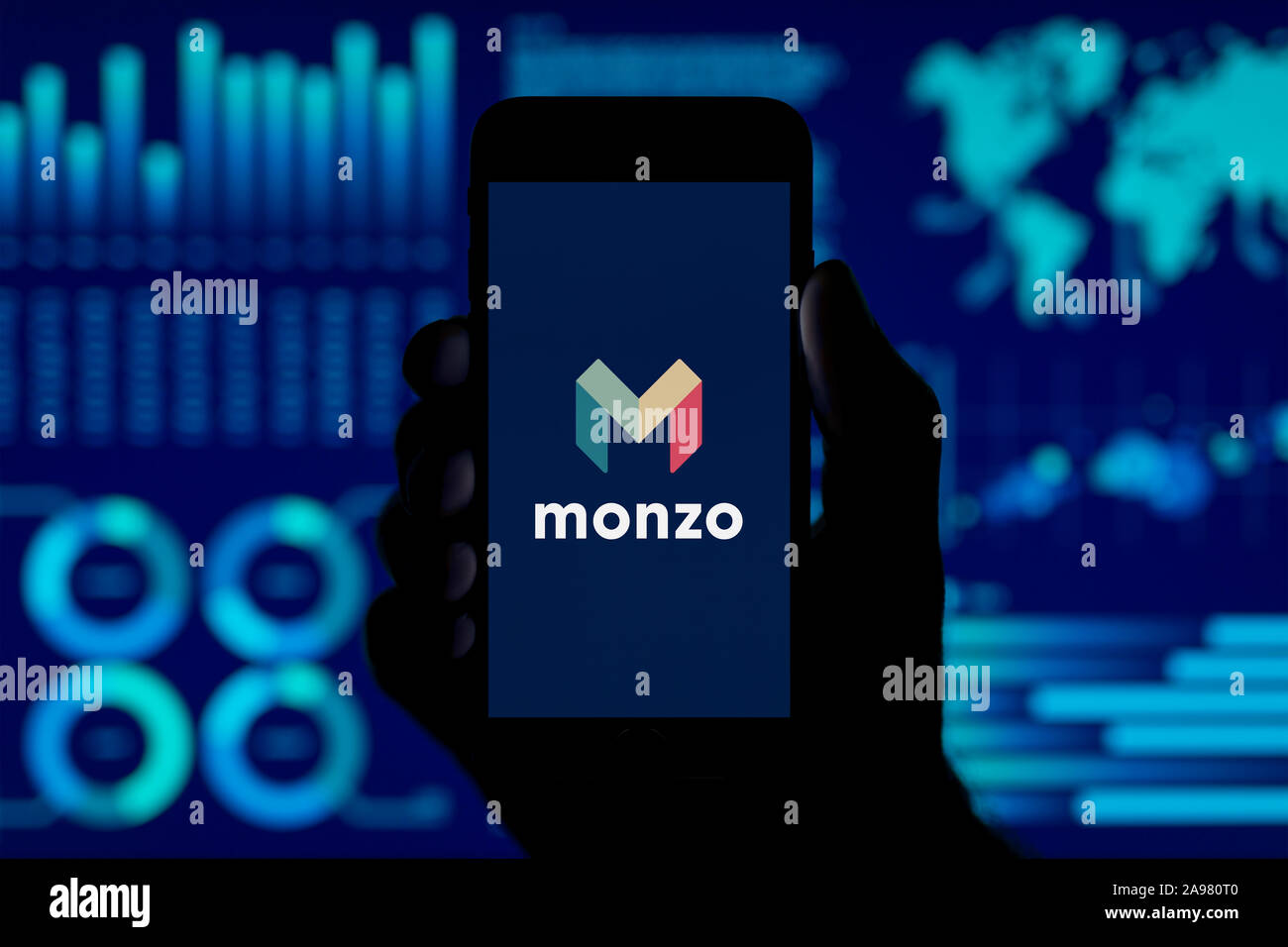 A man holds up an iPhone which displays the Monzo bank logo, shot ...