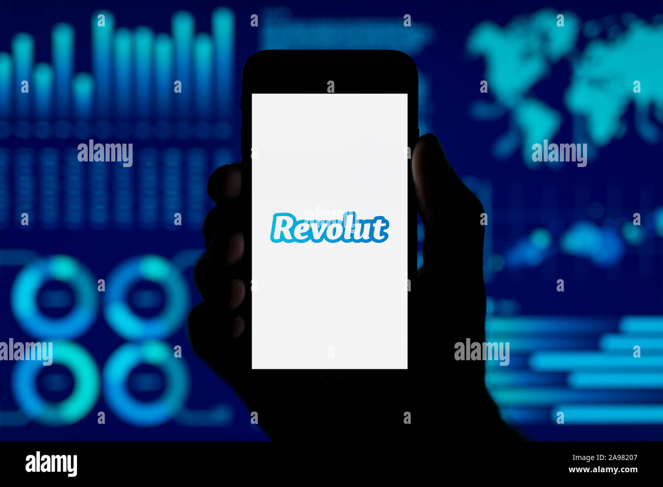 A man holds up an iPhone which displays the Revolut logo, shot against ...