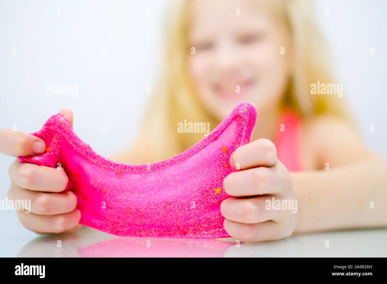 Blonde girl stretching pink glitter slime to the sides. Kids hands ...
