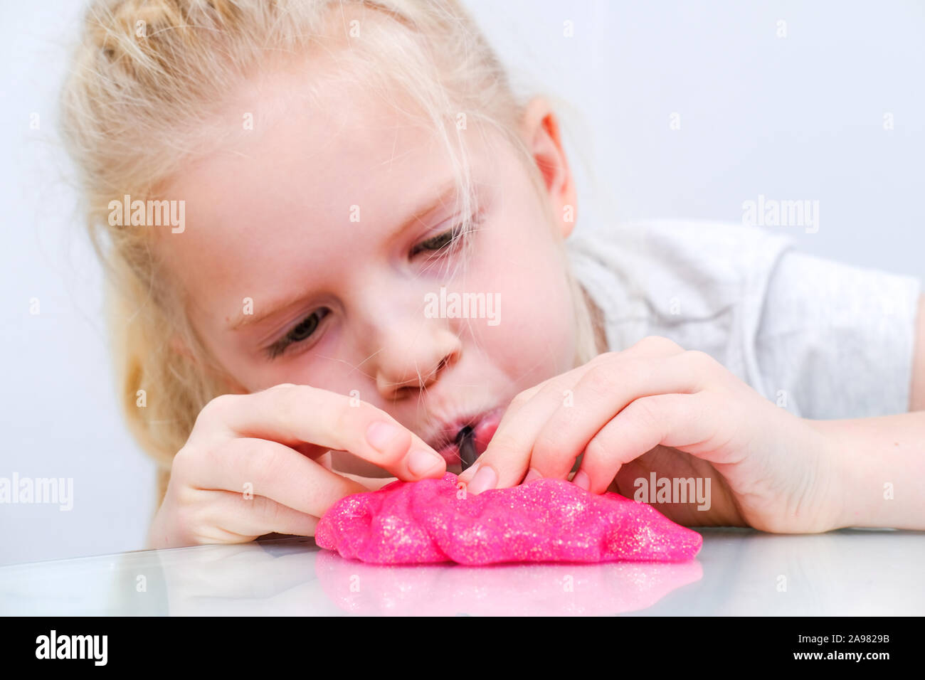 Blonde girl inflating bubble from pink glitter slime. Playing slime toy ...