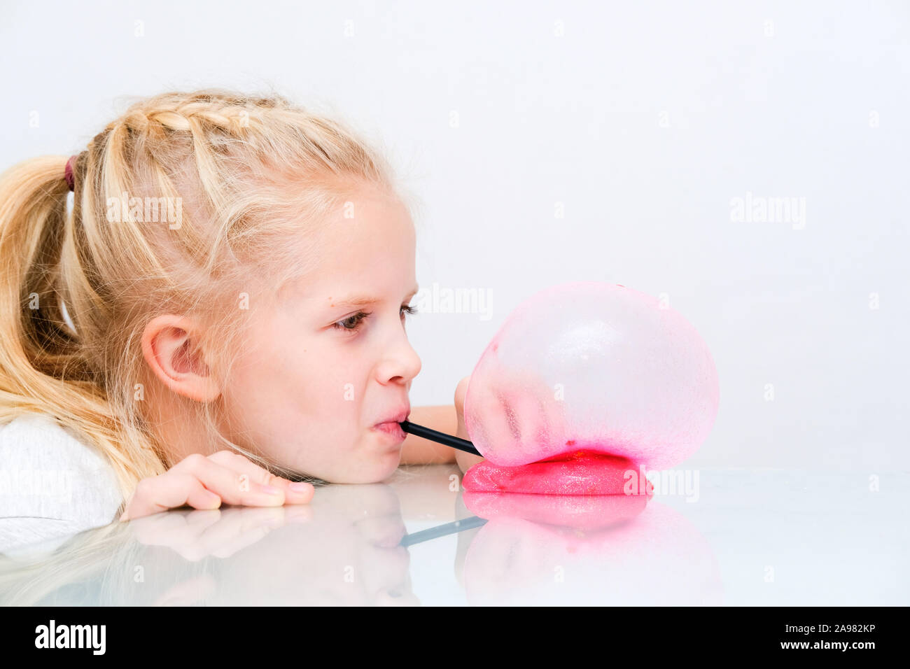 Blonde girl inflating bubble from pink glitter slime. Playing slime toy ...