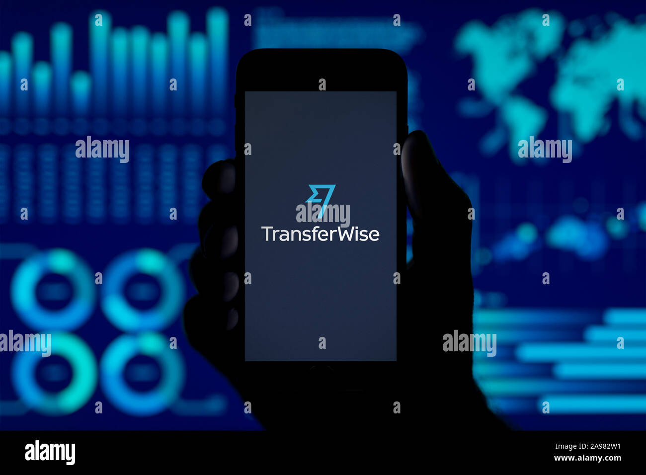 A man holds up an iPhone which displays the TransferWise logo, shot ...