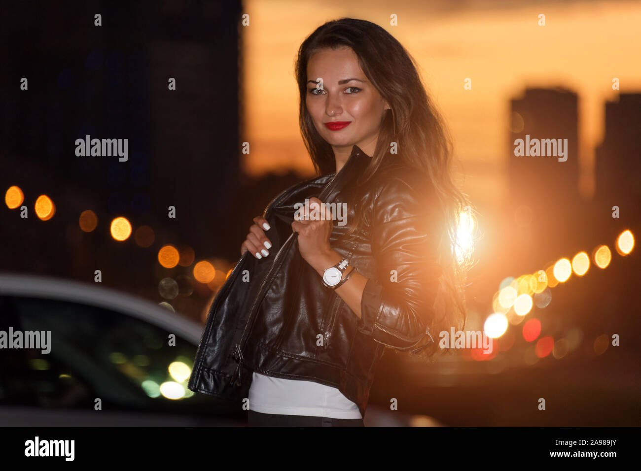 Beautiful young woman walking in the street with defocused city lights ...