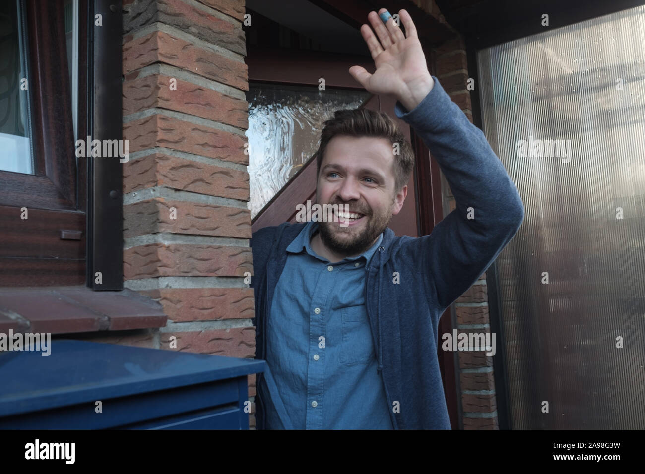 Smiling young man waving with a friendly cheerful smile to his new ...