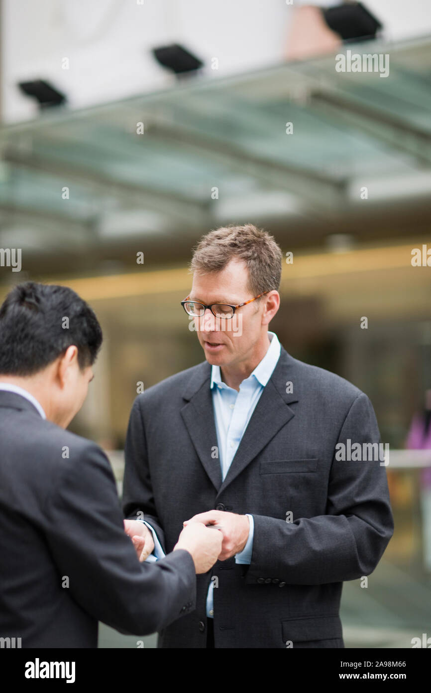 Two mid-adult businessmen exchanging business cards in the city Stock ...