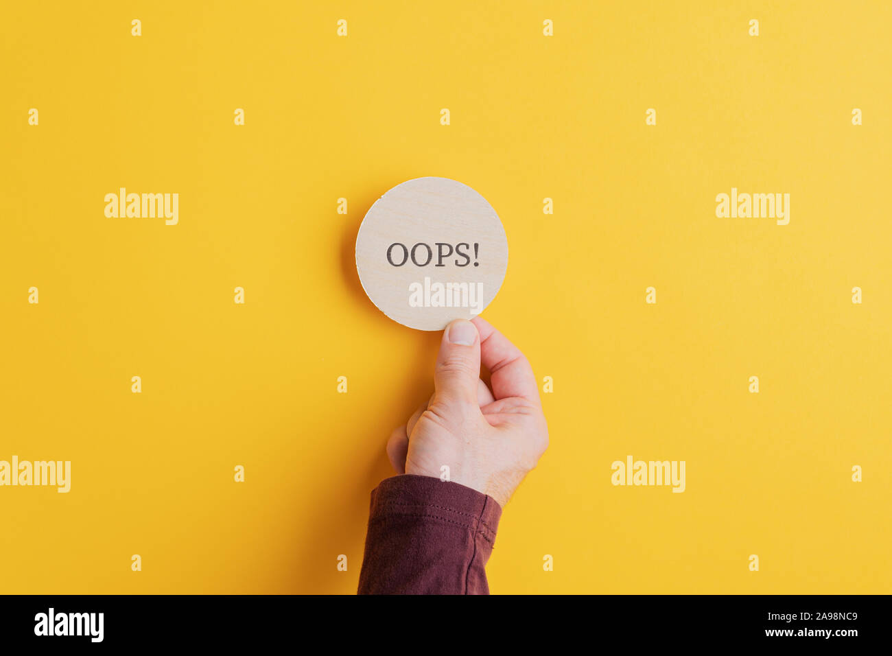 Male hand placing wooden cut circle with an Oops sign on it on bright ...
