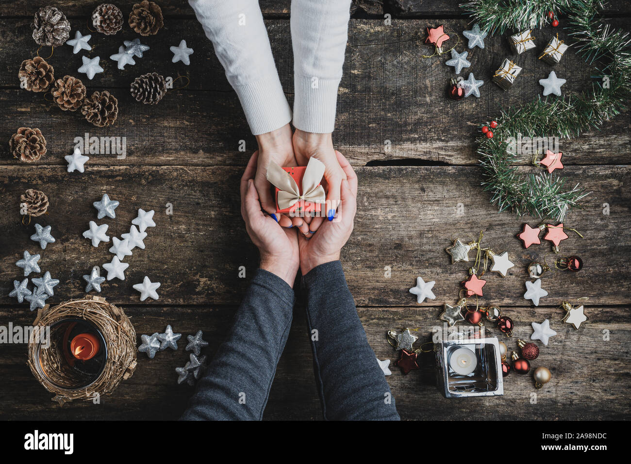 Top view of a male hands cupping female hands holding small red holiday ...