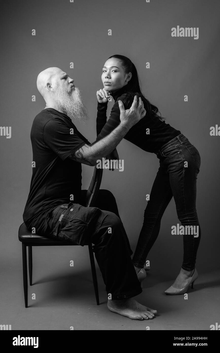 Mature bearded bald man with young Asian transgender woman together in ...
