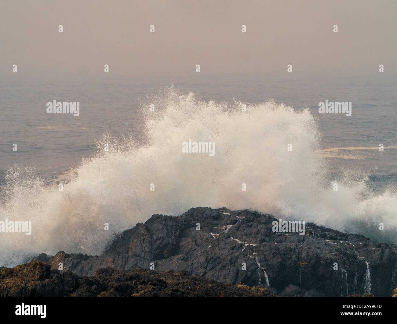 Smokey sky blurring the horizon line and waves crashing over rocks at ...