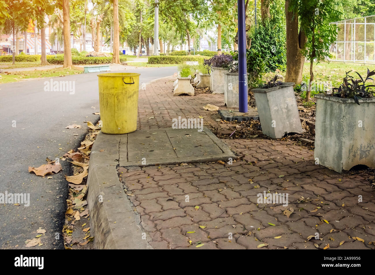 An old yellow dustbin in the public park beside the walk way for ...