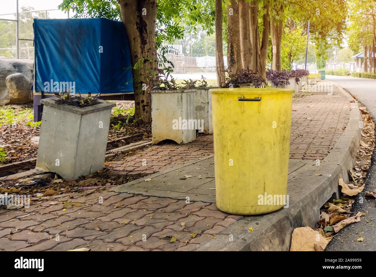 An old yellow dustbin in the public park beside the walk way for ...