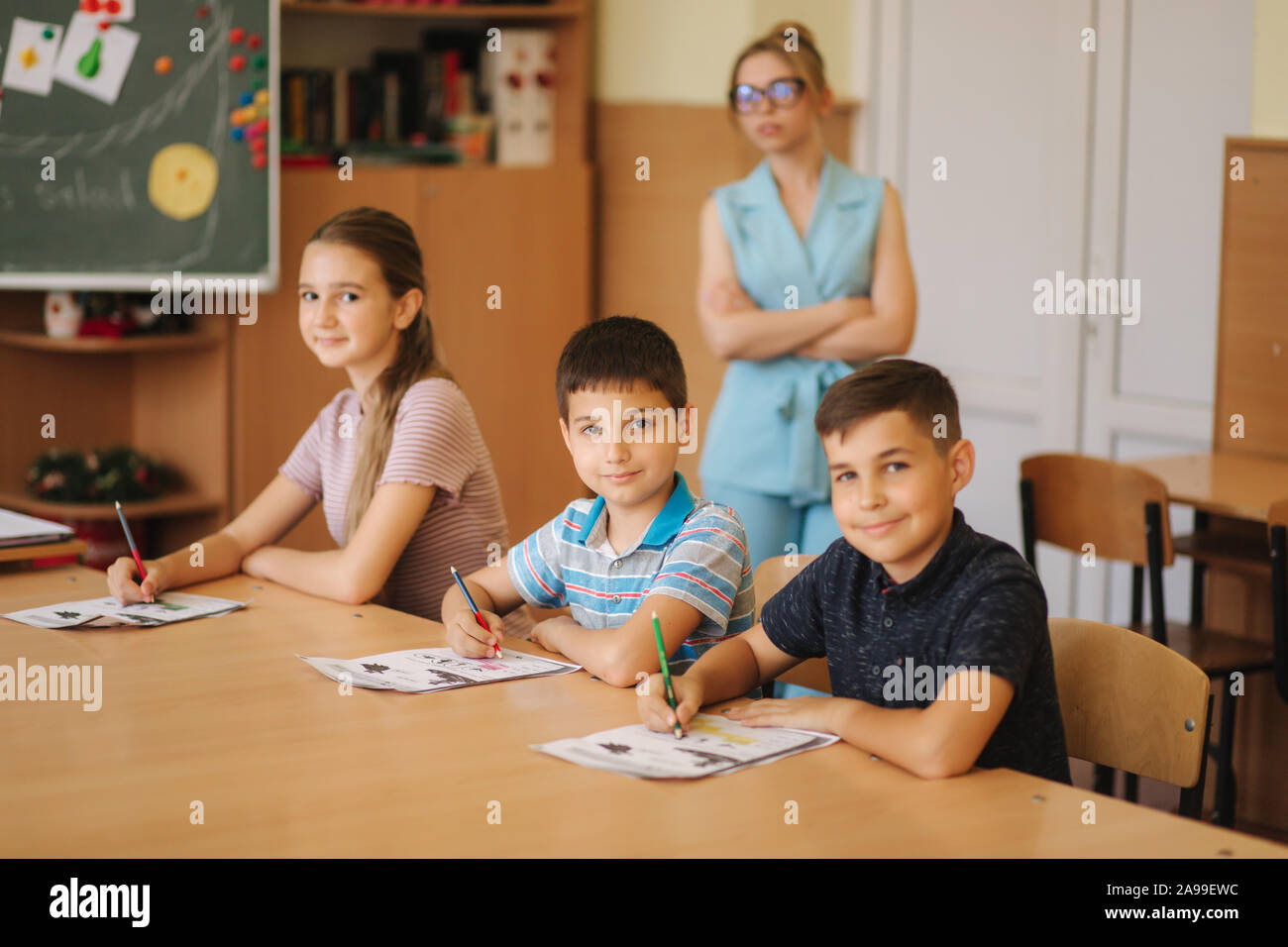 Teacher helping school kids writing test in classroom. education ...