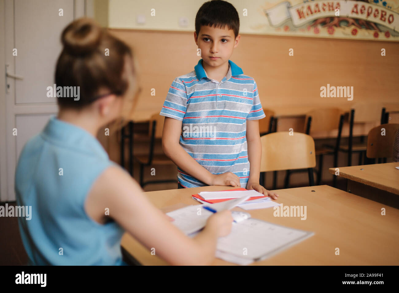Pretty teacher in classroom sitting at the desk and asking children ...