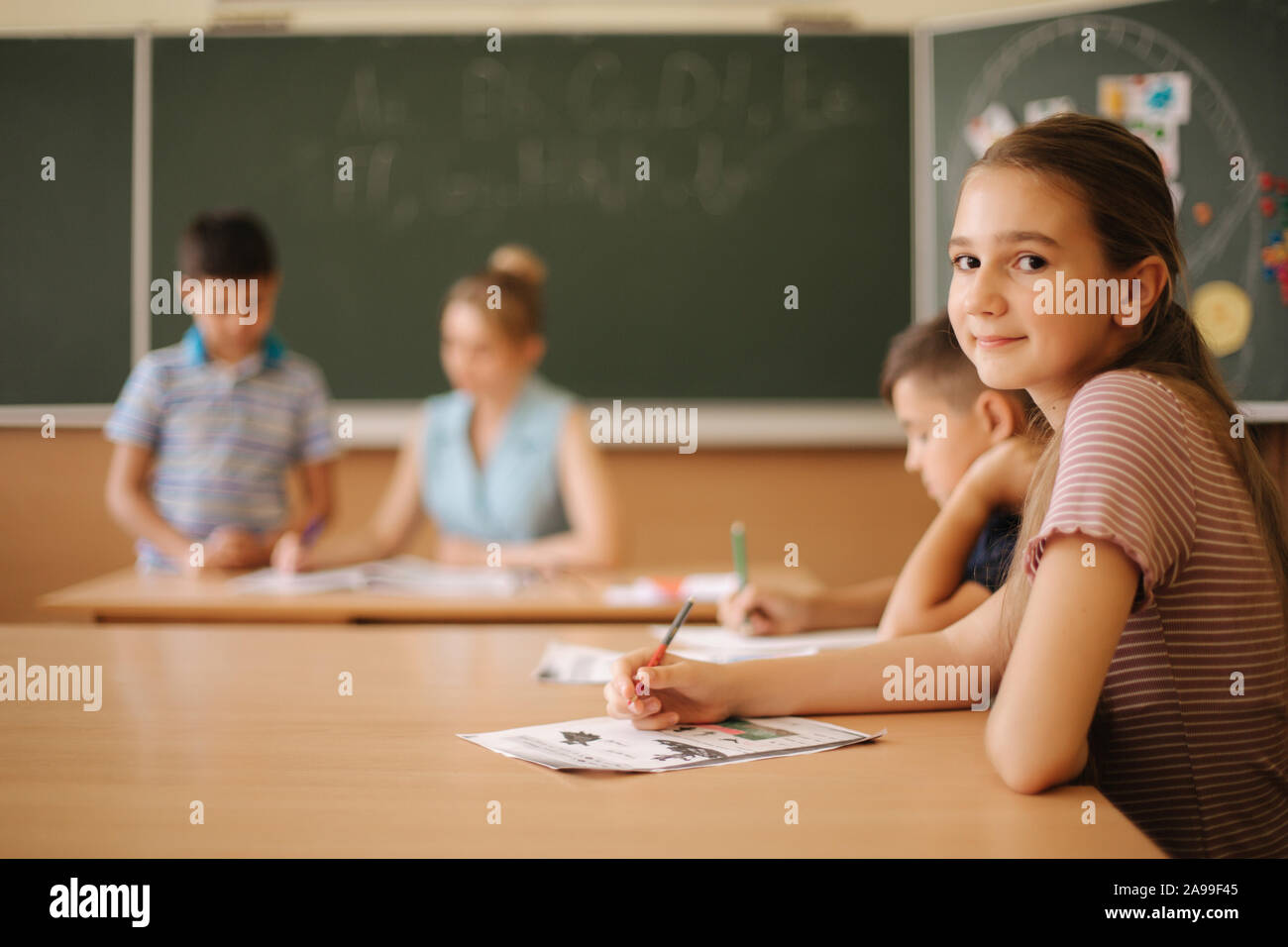 Group of school kids with pens and notebooks writing test in classroom ...