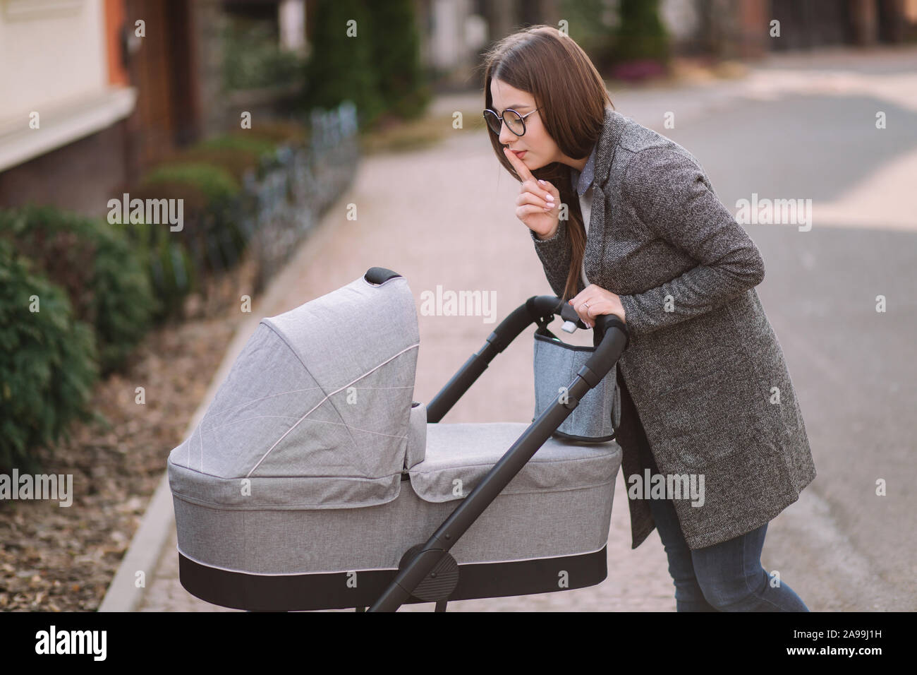Young mother walking with her baby in stroller and putting finger up to ...