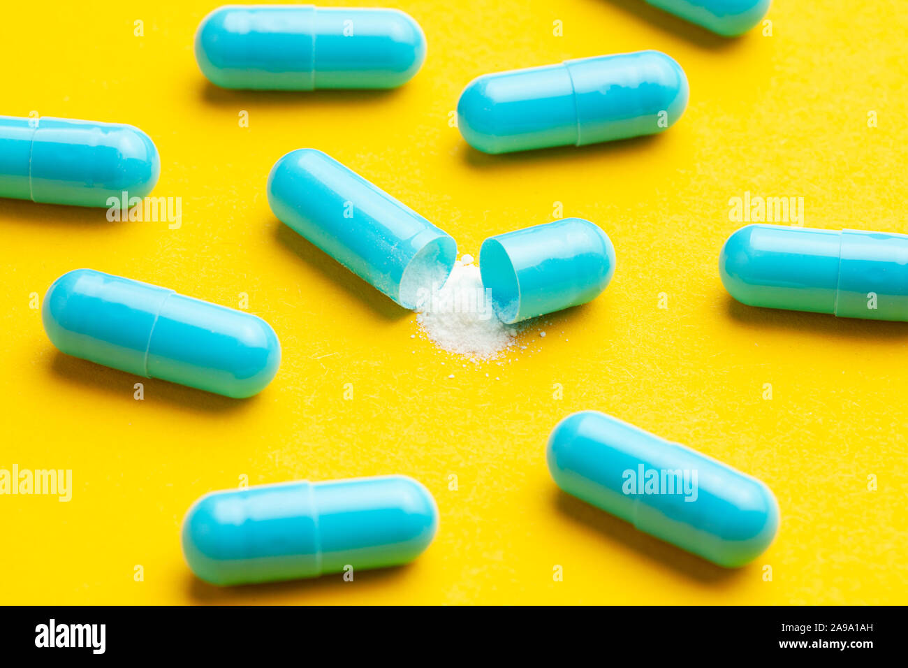 Blue tablets in capsules. One capsule is open. Yellow background Stock ...
