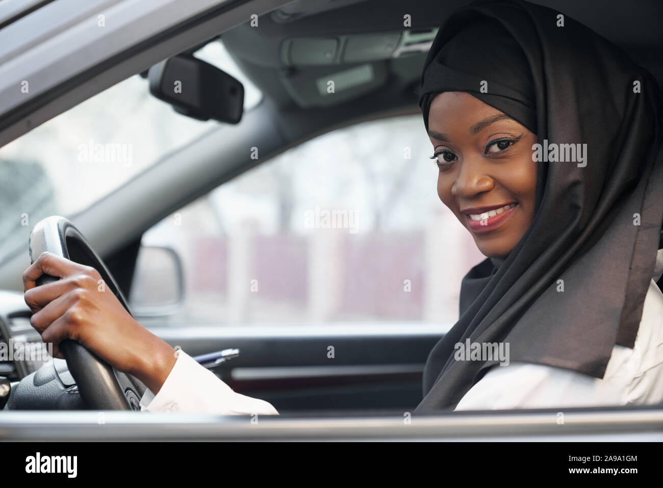 Side view of beautiful woman in black hijab and looking at camera while ...