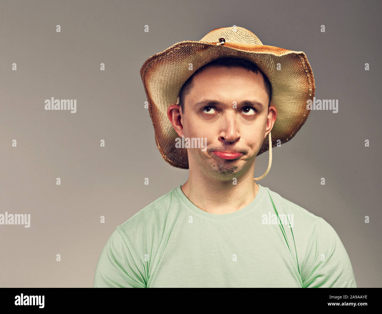 Thinking resentful man showing facial grimace in summer hat on grey ...