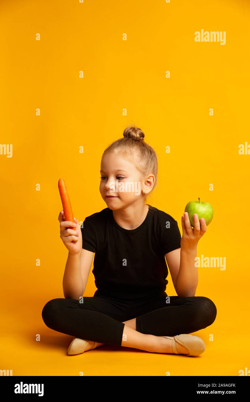 Puzzled little dancer choosing between carrots and green apple Stock ...