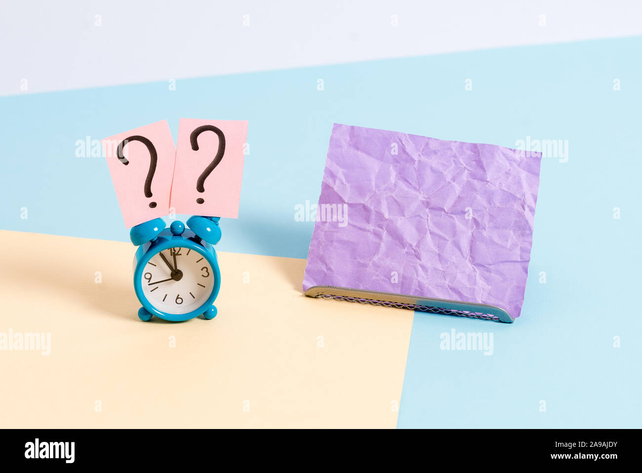 Mini size alarm clock beside a Paper sheet placed tilted on pastel ...