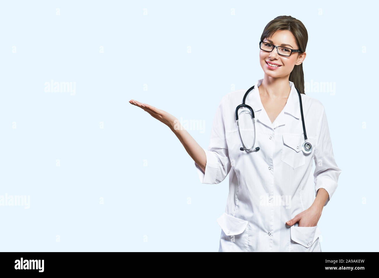 Friendly smiling young female doctor. hand pointing at copy space ...