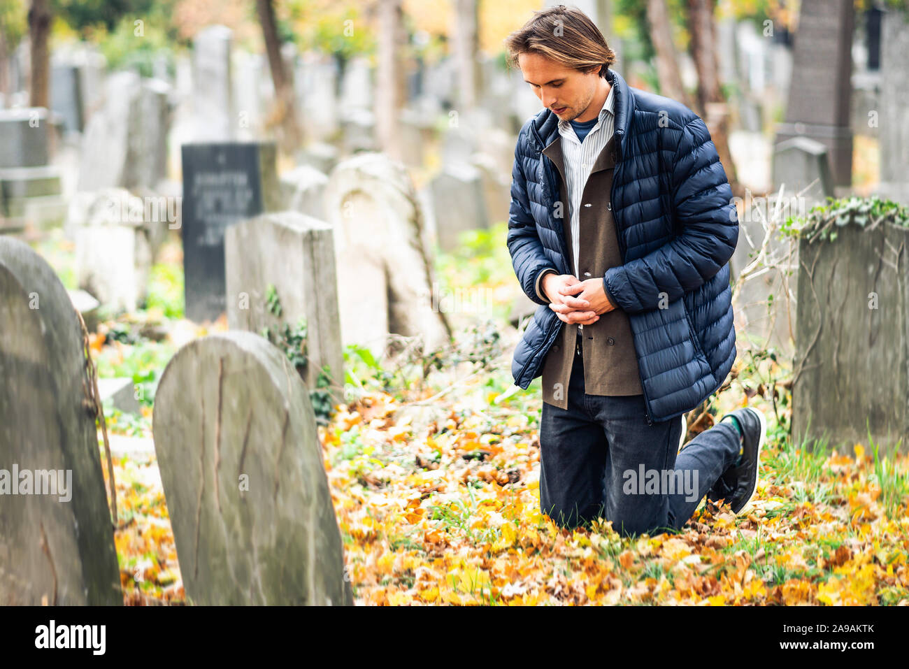 Mourning young man kneeling in front of a grave on a cemetery during a ...