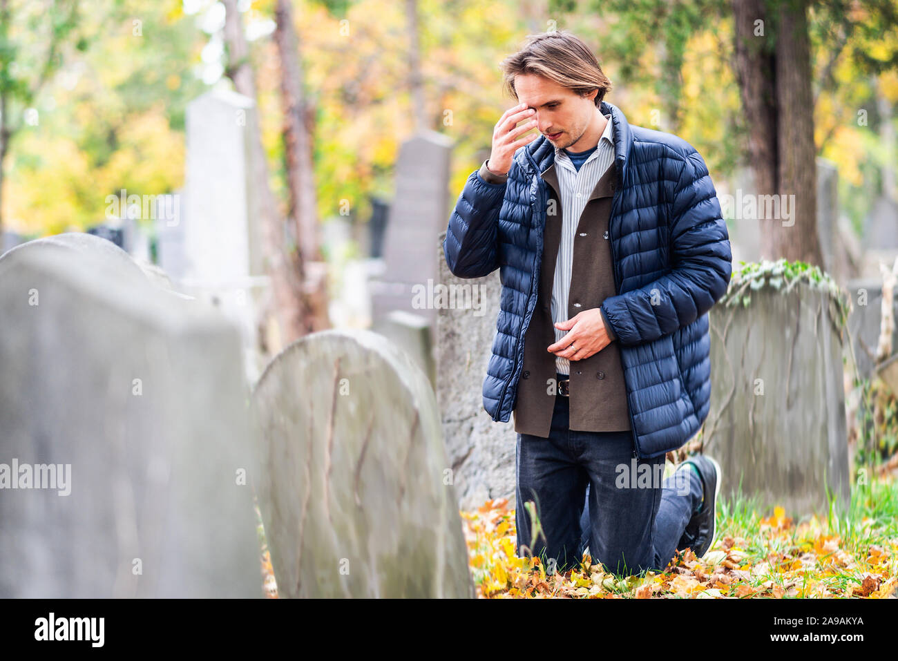 Mourning young man kneeling in front of a grave on a cemetery during a ...