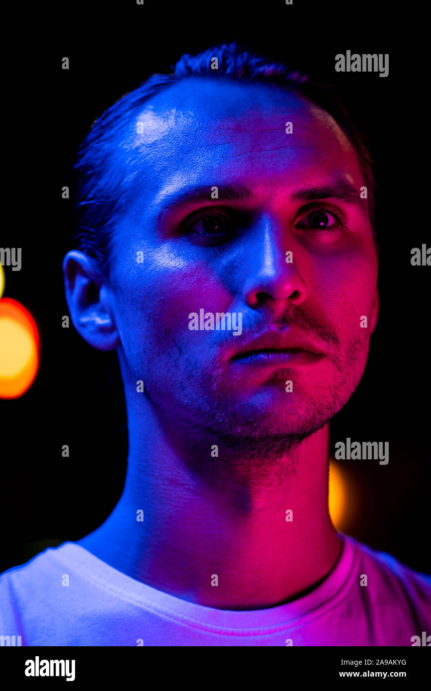 Modern red and blue light portrait of a young man. Streetlights visible ...
