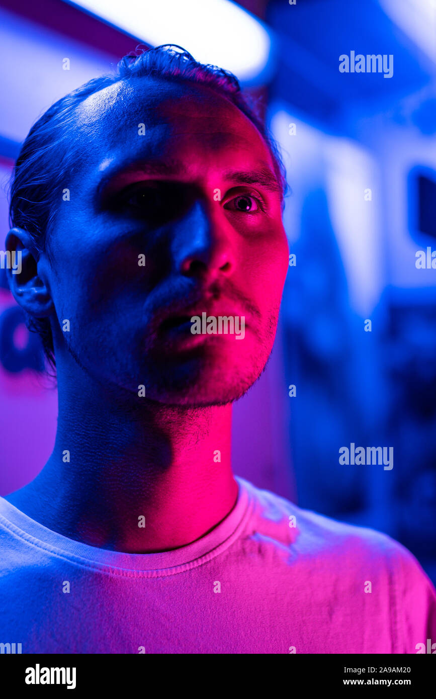Modern red and blue light portrait of a young man. Streetlights visible ...