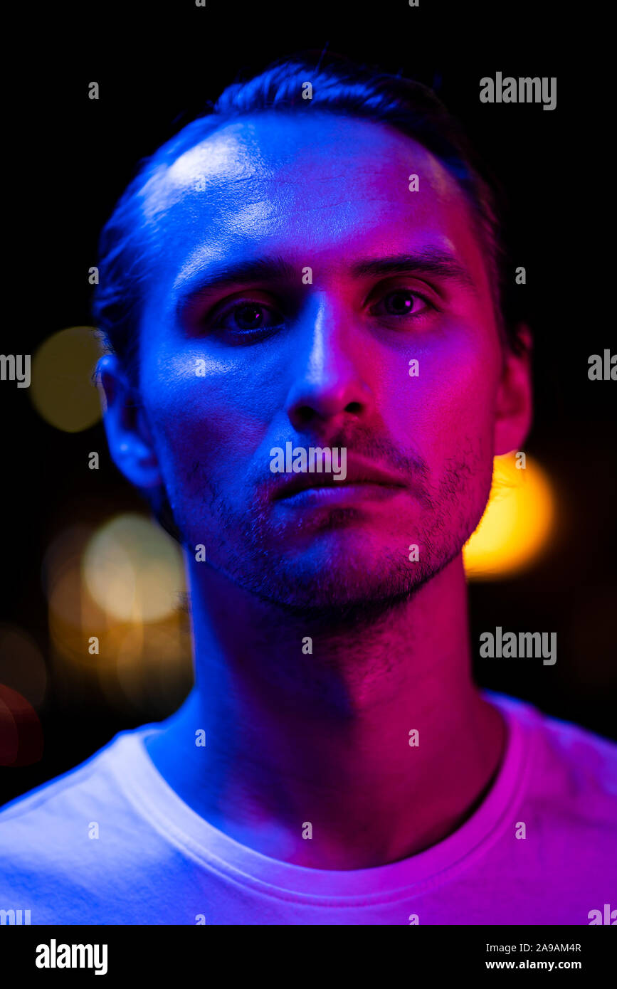 Modern red and blue light portrait of a young man. Streetlights visible ...